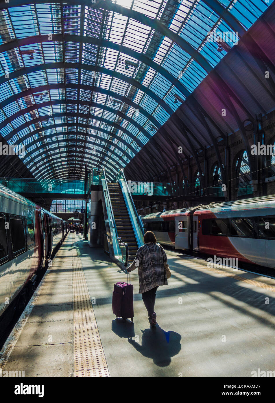 A woman pushing a suitcase along the platform, in strong sunlight ...