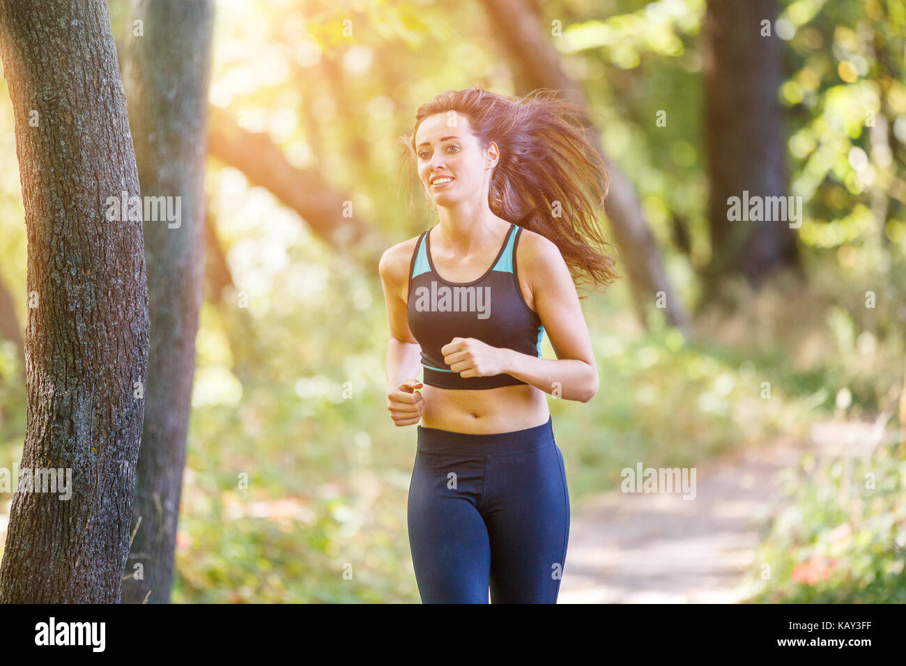 Young smiling sporty woman running in park in the morning. Fitness girl jogging in park. Trail ...