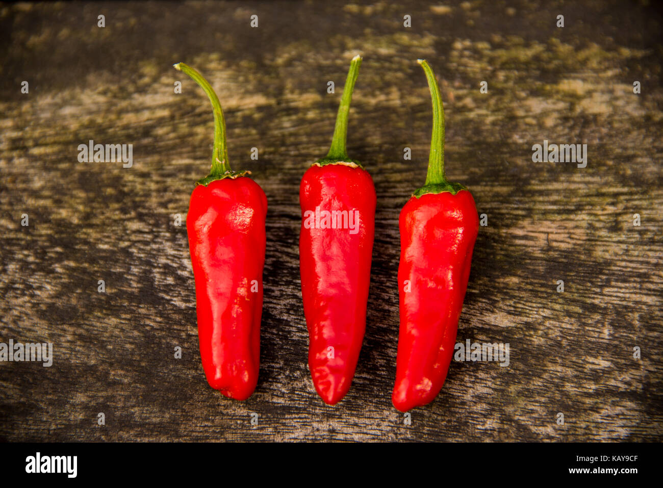 Three Red Chilli Peppers on a Wooden Background Stock Photo - Alamy