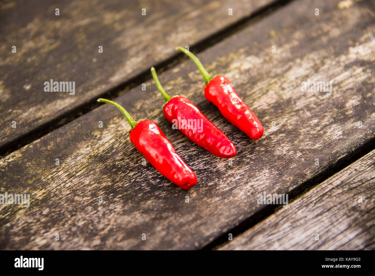 Three Red Chilli Peppers on a Wooden Background Stock Photo - Alamy
