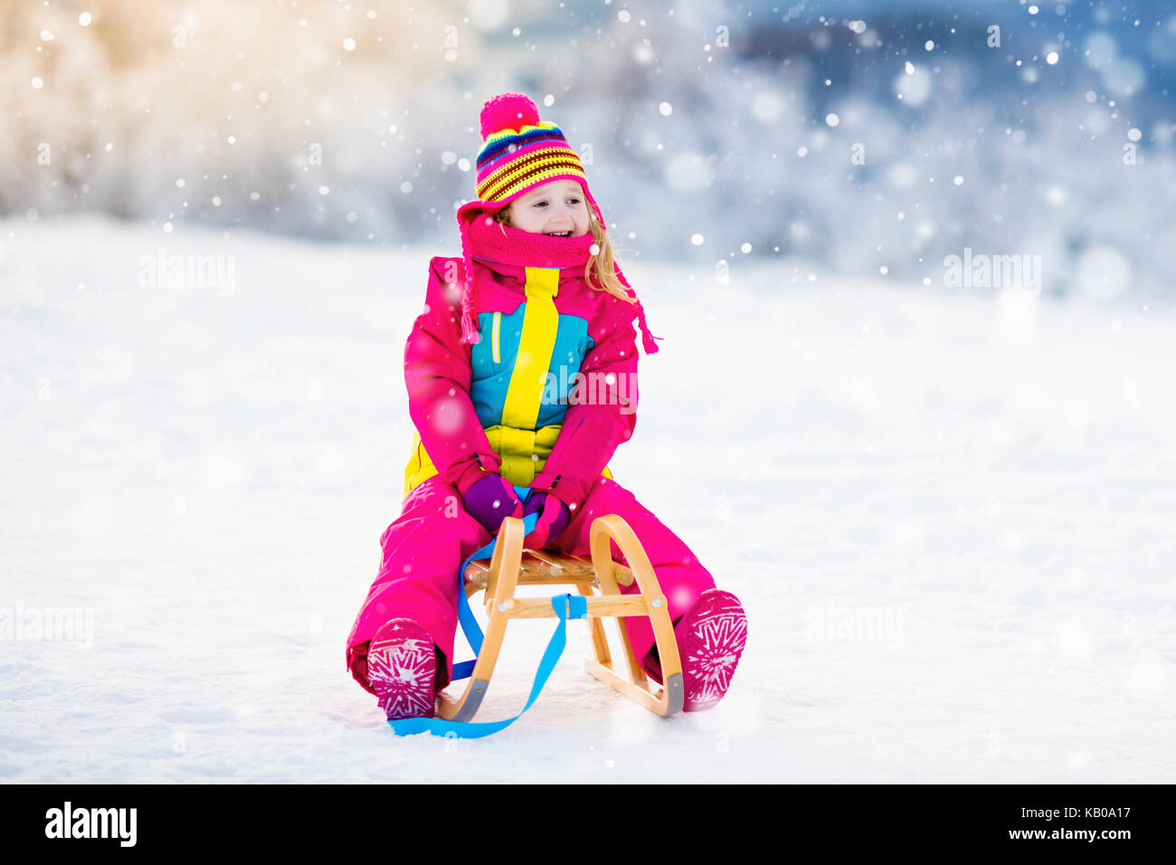 Little girl enjoying a sleigh ride. Child sledding. Toddler kid riding a sledge. Children play ...