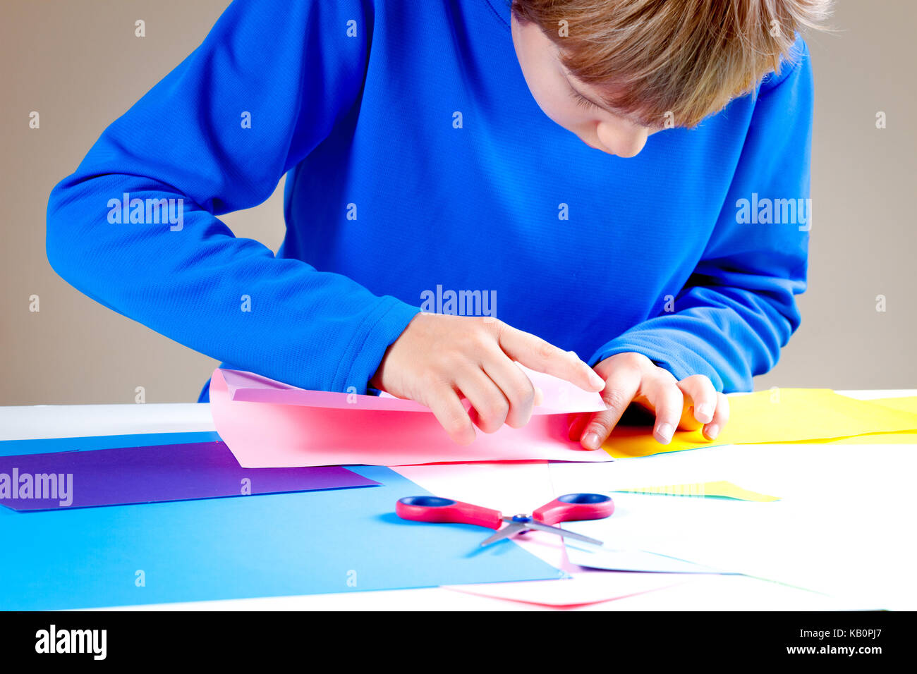 Kid folding colored paper and making origami Stock Photo - Alamy