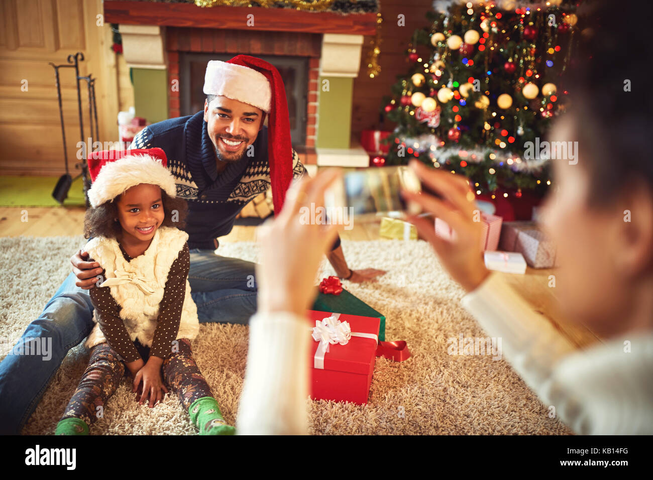 mother taking picture of smiling father and daughter in Santa hats at ...