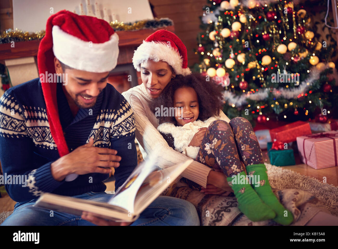 Happy family reading book at home by fireplace in warm and cozy living ...