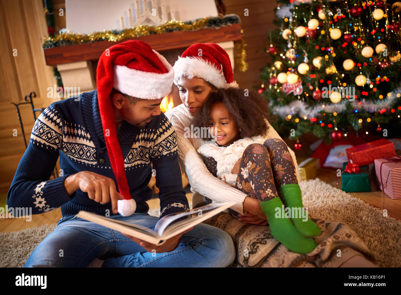 Handsome young dad reading a book to his cute daughter near Christmas ...
