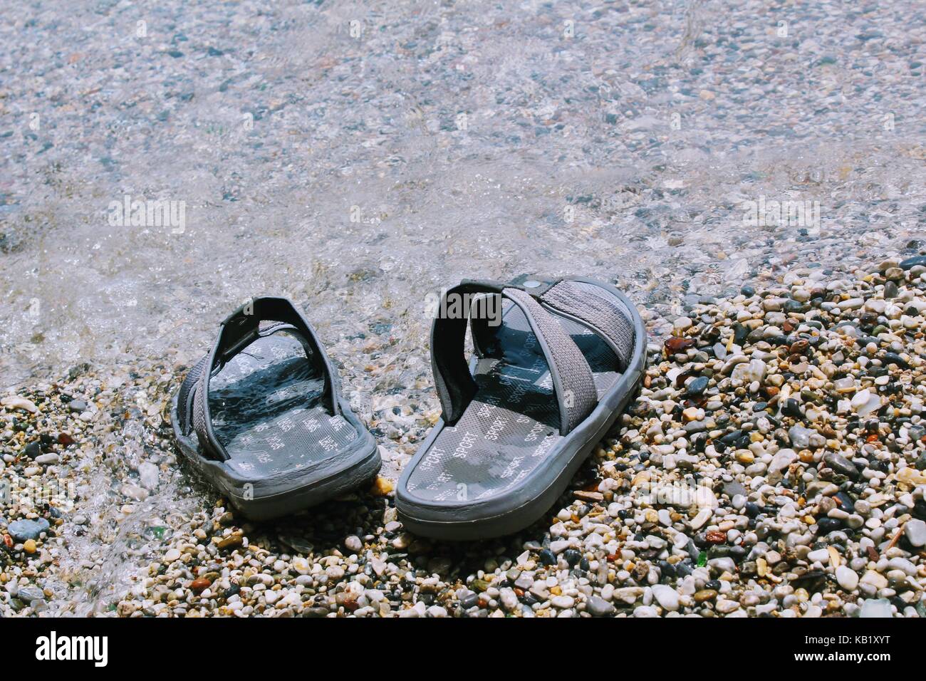 Men's beach slippers lie on the pebbles in the surf zone. They are ...