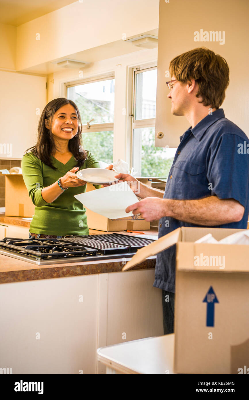 A young couple in their kitchen unpacking plates from moving boxes ...