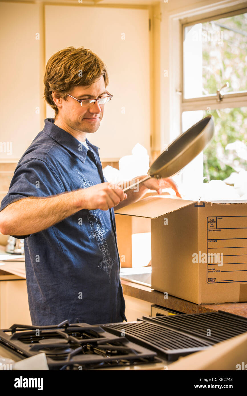 A Caucasian young man packing / unpacking a pan in his kitchen as if ...