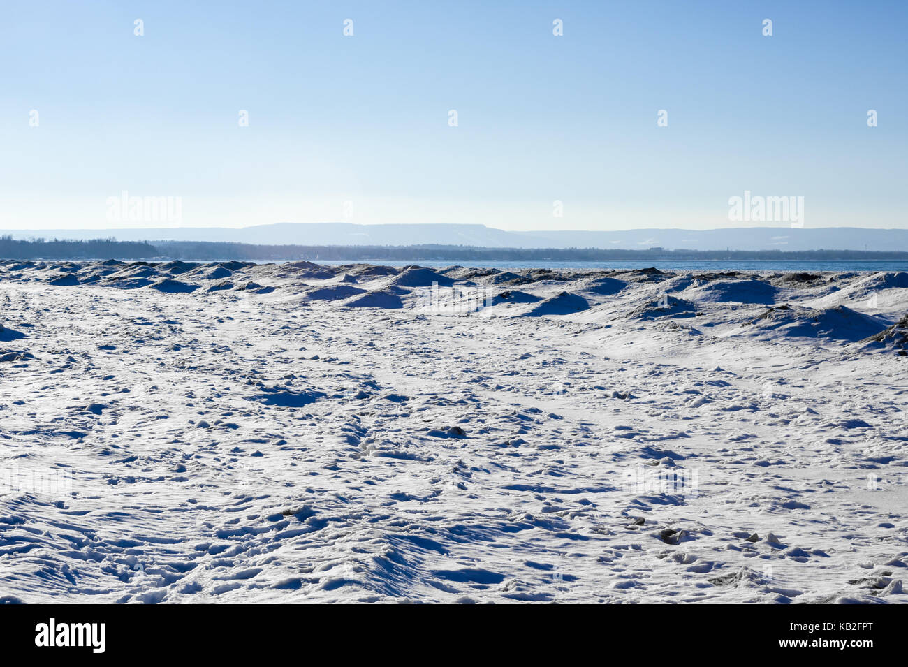 frozen ice, snow, and sand dunes on beach in winter by lake under clear ...