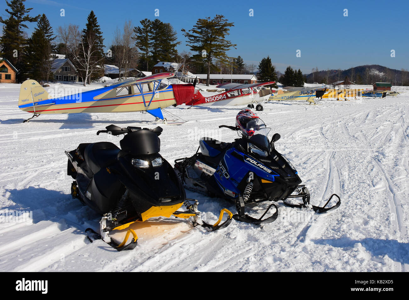 Two snowmobiles parked on Lake Pleasant, NY, with a line of ski planes ...