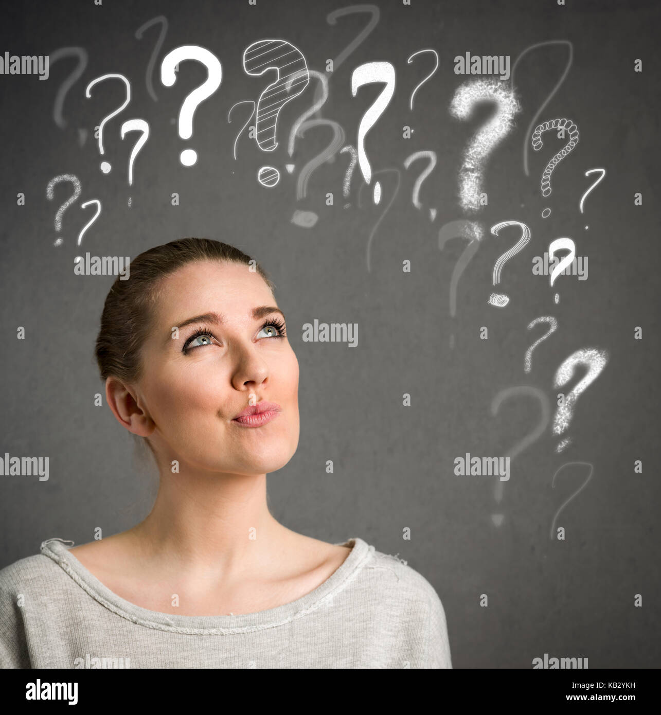 Young woman makes a face and thinking with question marks over head ...