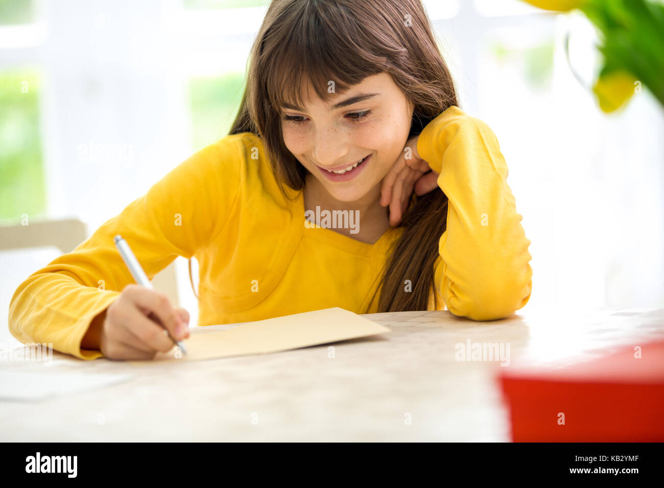 Cute smiling girl writing a letter sitting at desk Stock Photo - Alamy