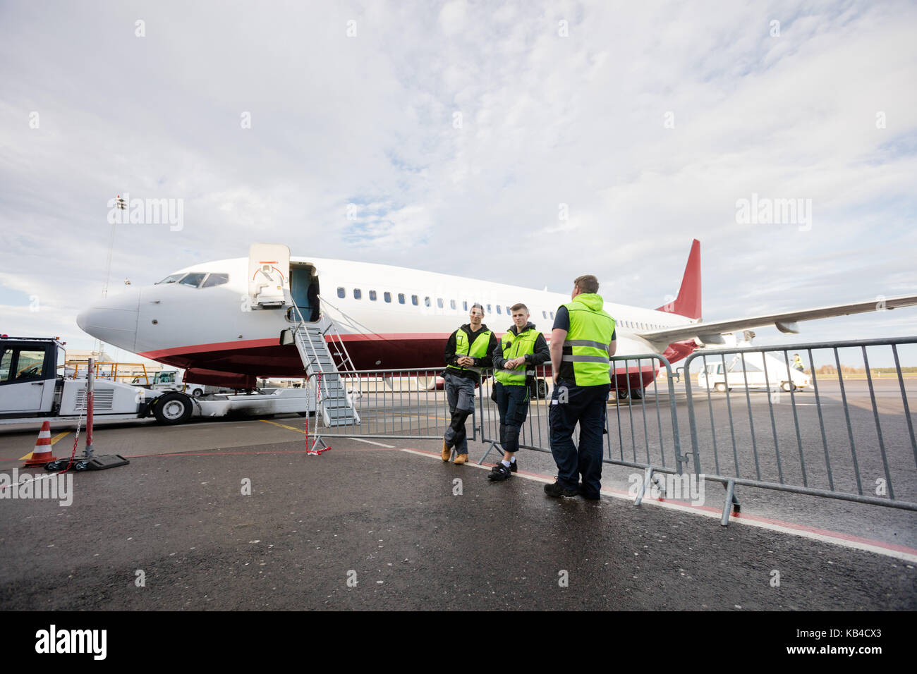Full length of male ground crew standing by fence against airplane on ...