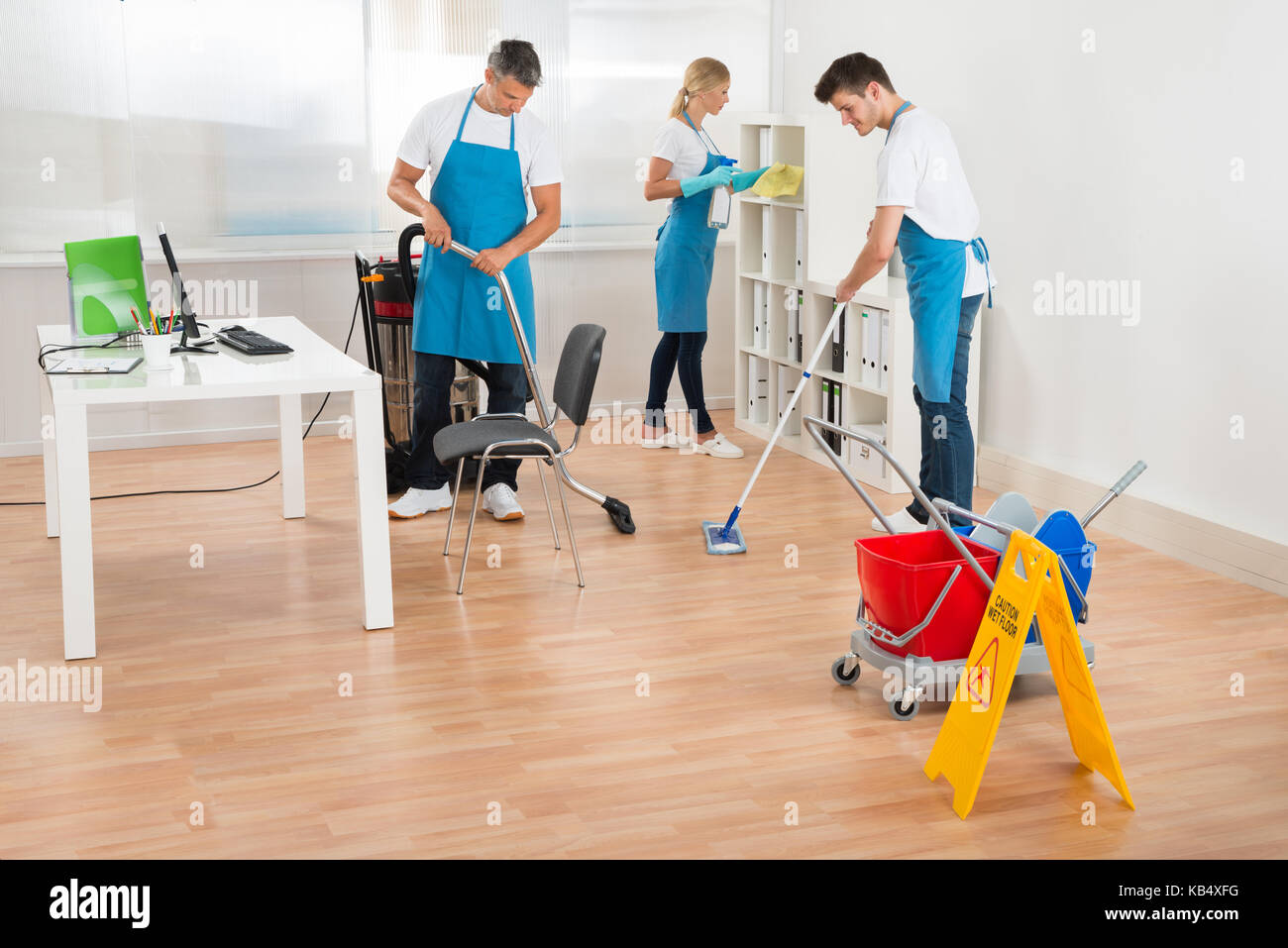 Group Of Three Janitors In Blue Apron Cleaning Office Stock Photo - Alamy