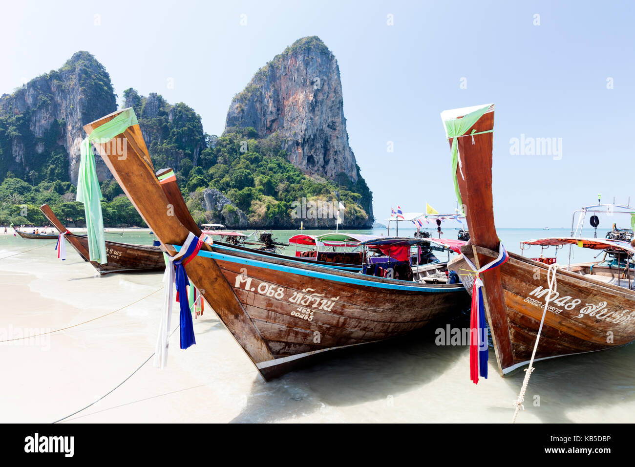 Traditional Longtail boats moored by Railay Beach with limestone cliffs ...