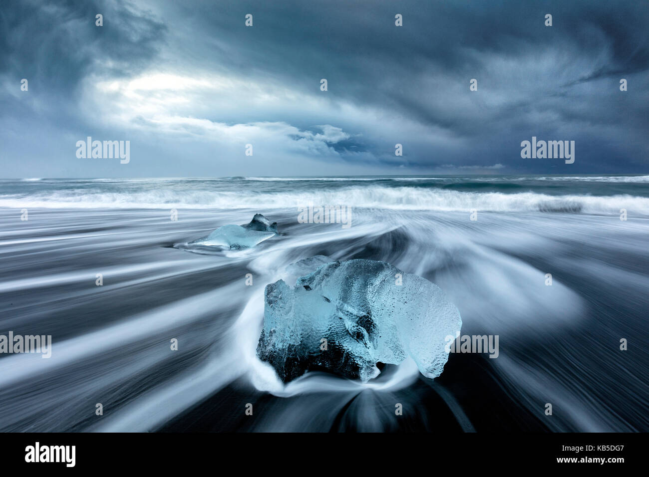 Glacier ice on black sand beach with waves washing up the beach on a ...