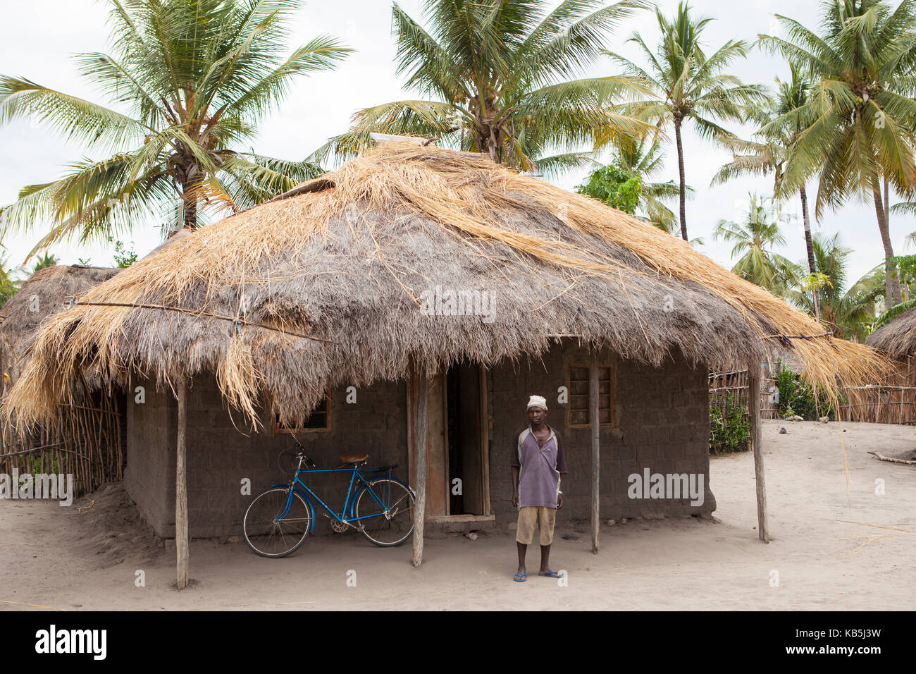 A man stands proudly outside his traditional mud hut home which has ...