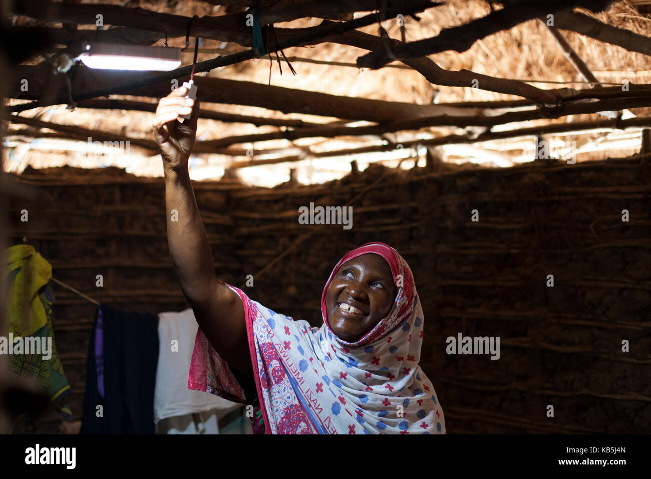 A woman smiling as she turns on the new solar light in her mud hut ...