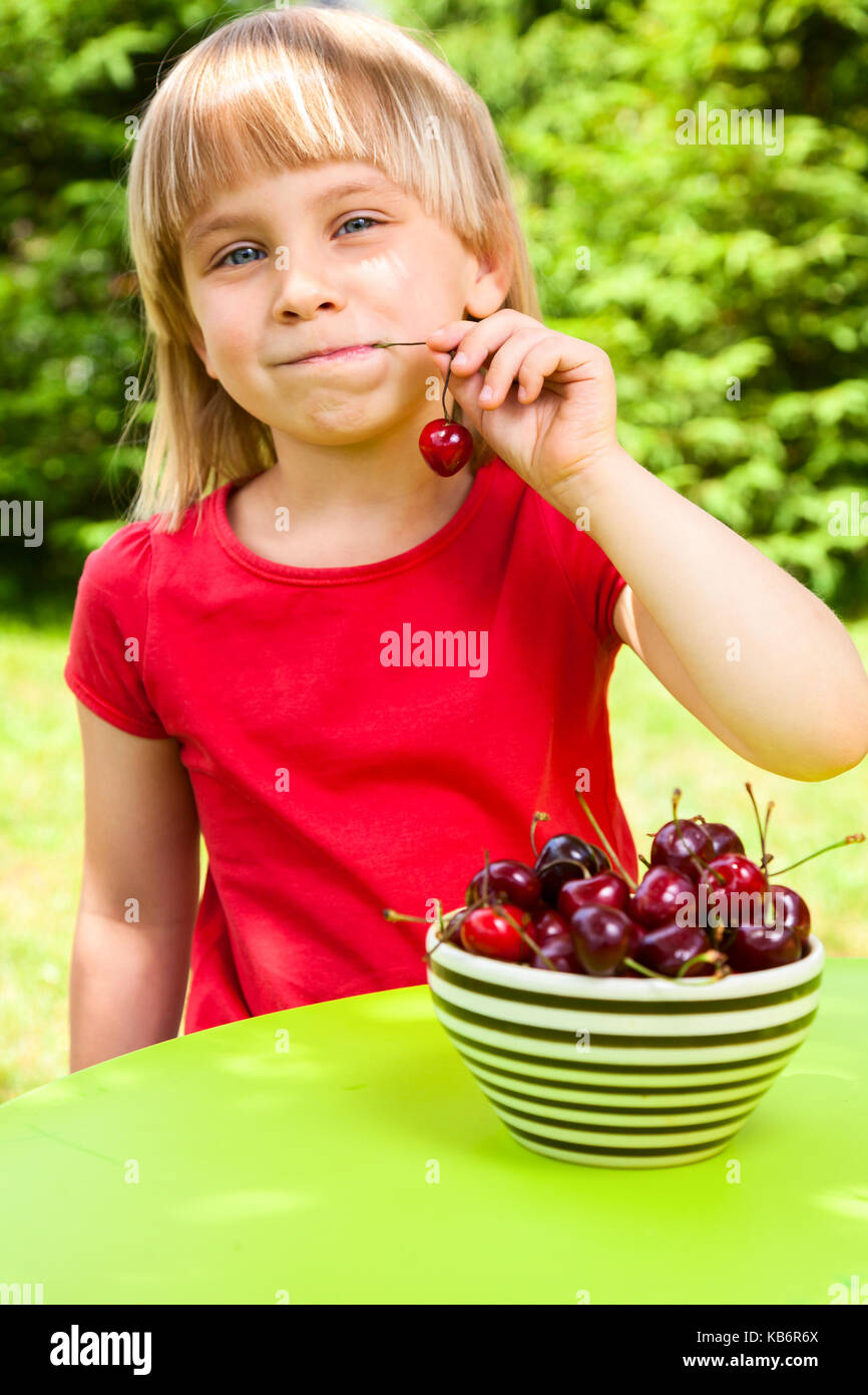 Cute little girl eating sweet cherry outdoors Stock Photo - Alamy