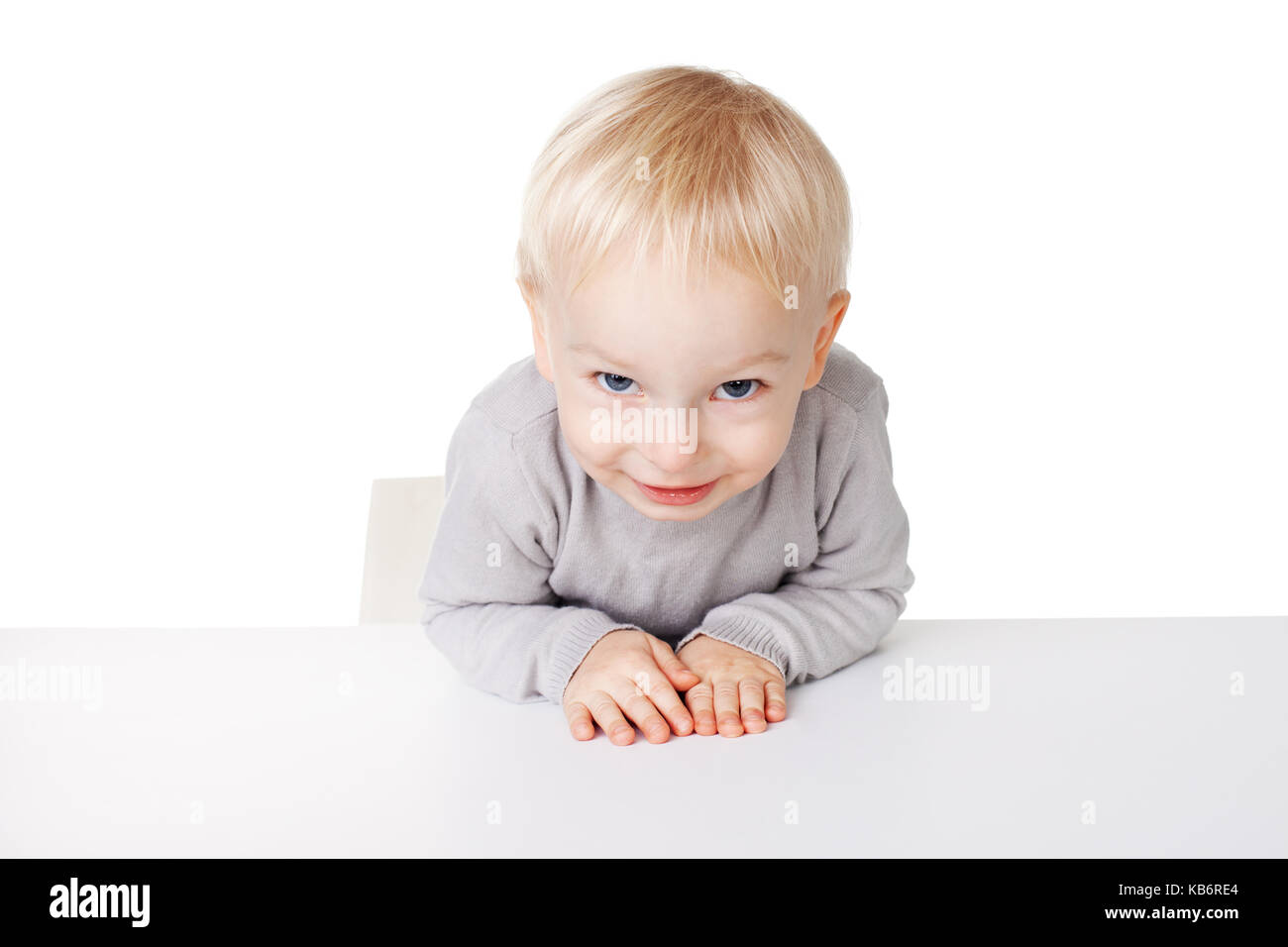 Cute little smiling boy sitting at table isolated on white background ...