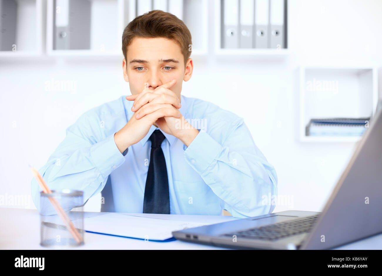 Portrait of young pensive businessman at his workplace in bright office ...