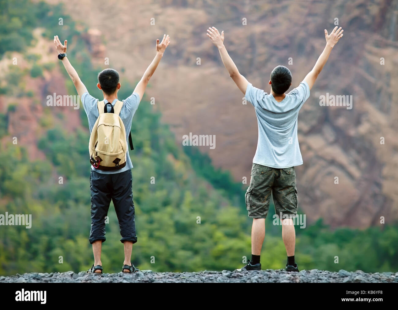Two young tourist men standing with raised hands on rocky cliff Stock ...