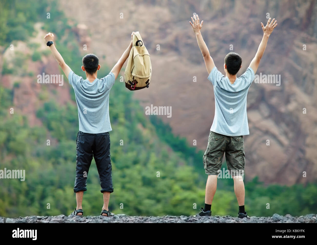 Two young tourist men standing with raised hands on rocky cliff Stock ...