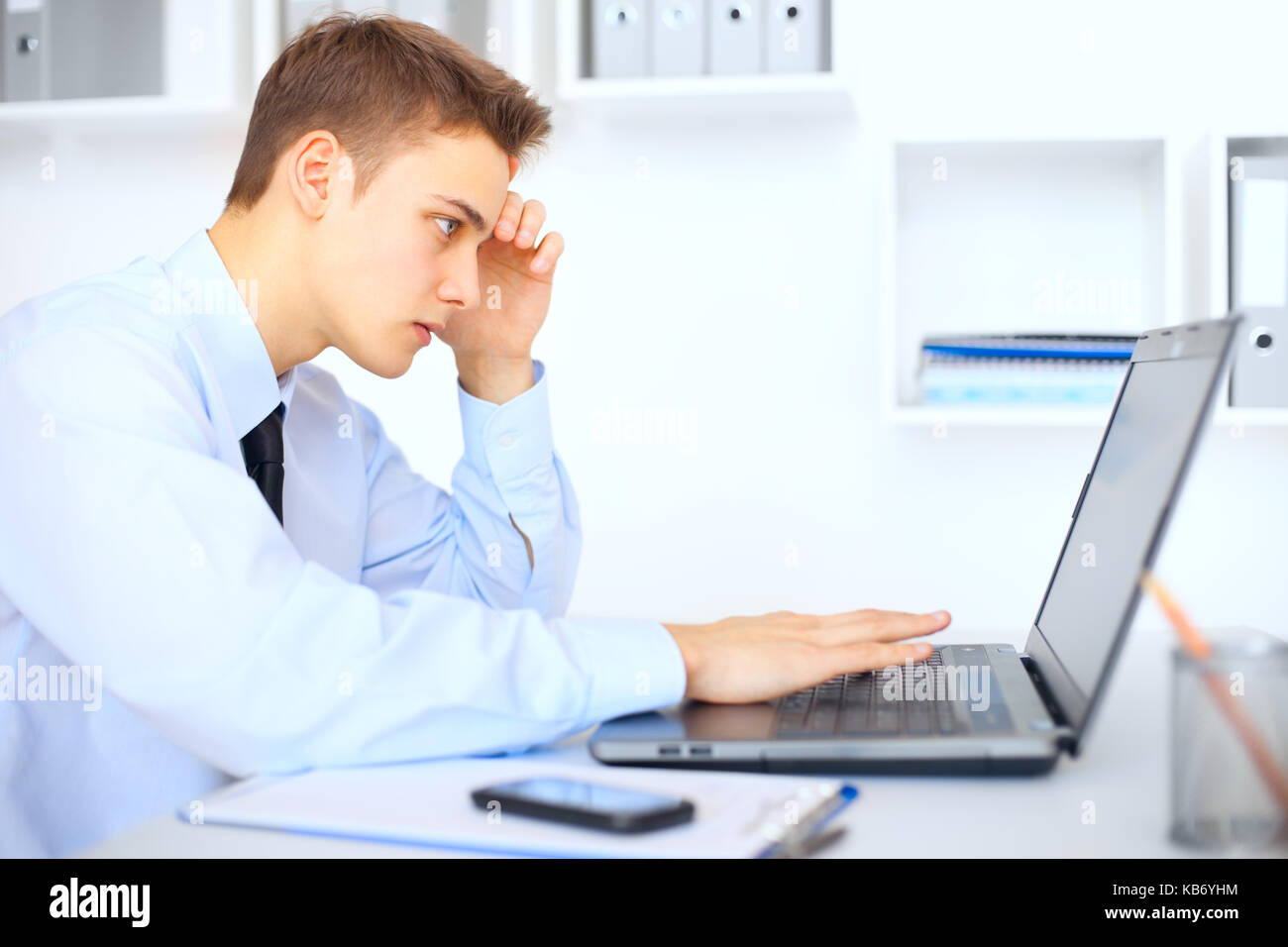 Side view young serious businessman working on laptop in bright office ...