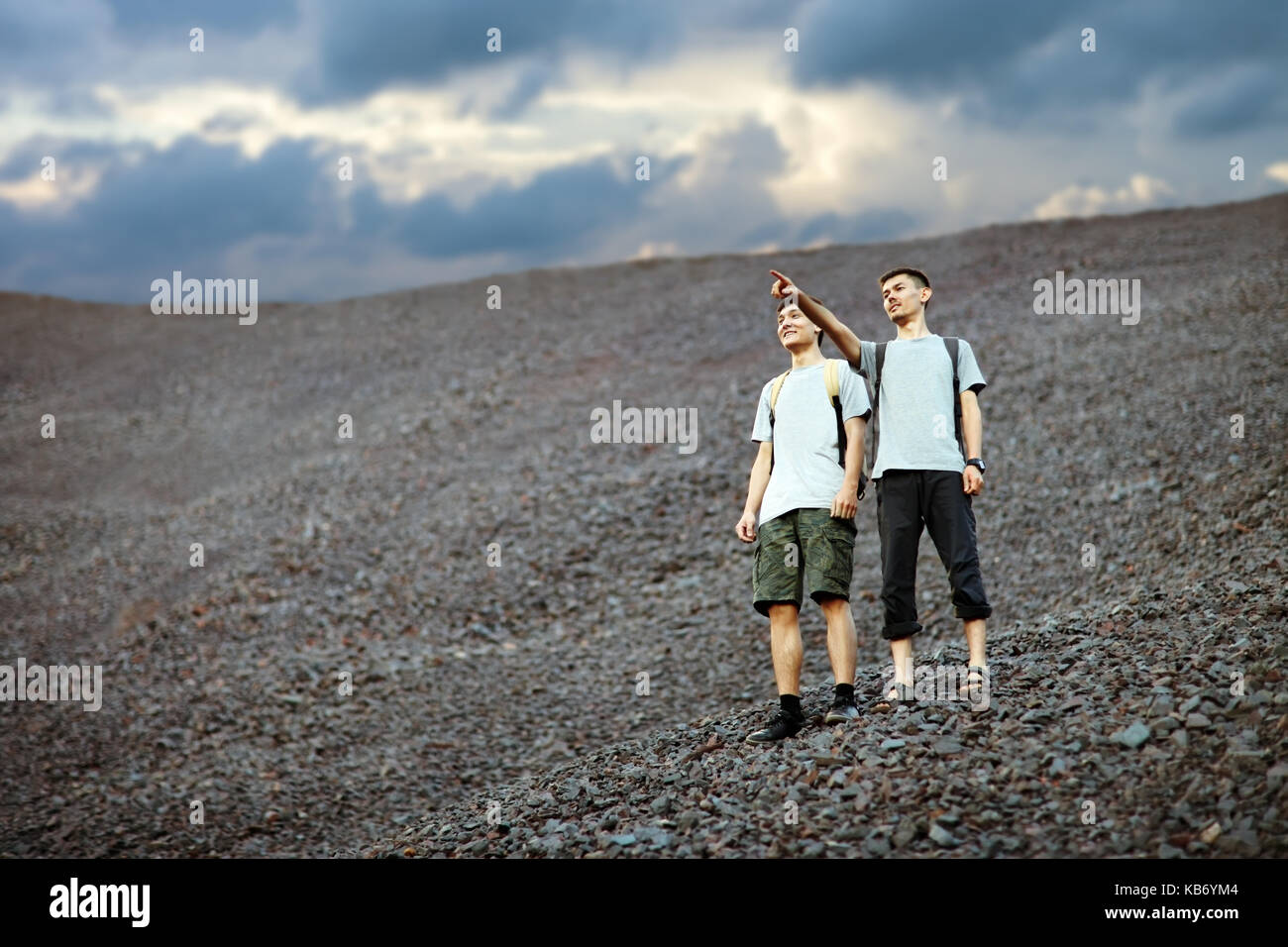 Two young men standing on stones and rock slope and pointing away Stock ...