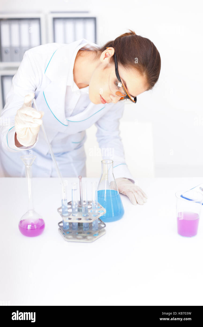 Young chemical female researcher with vials and flasks makes some experiments in laboratory ...