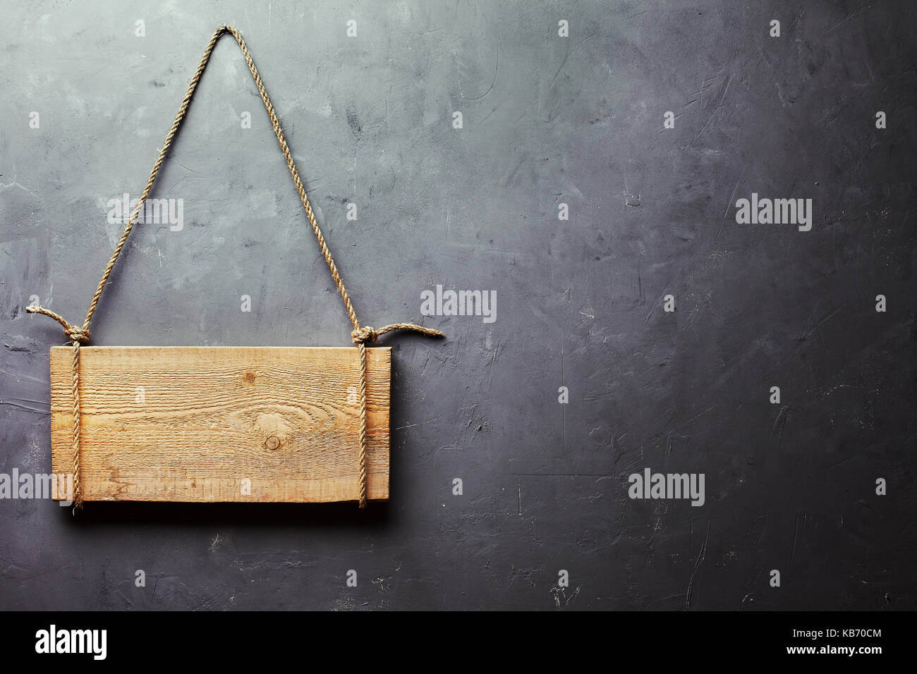 Wooden signboard hanging on rope on gray textured wall with copy space ...