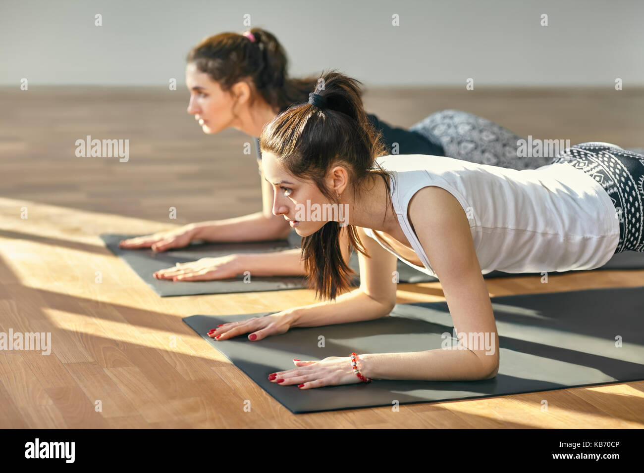 Two young women doing yoga asana Low Plank Pose. Ardha Phalakasana ...