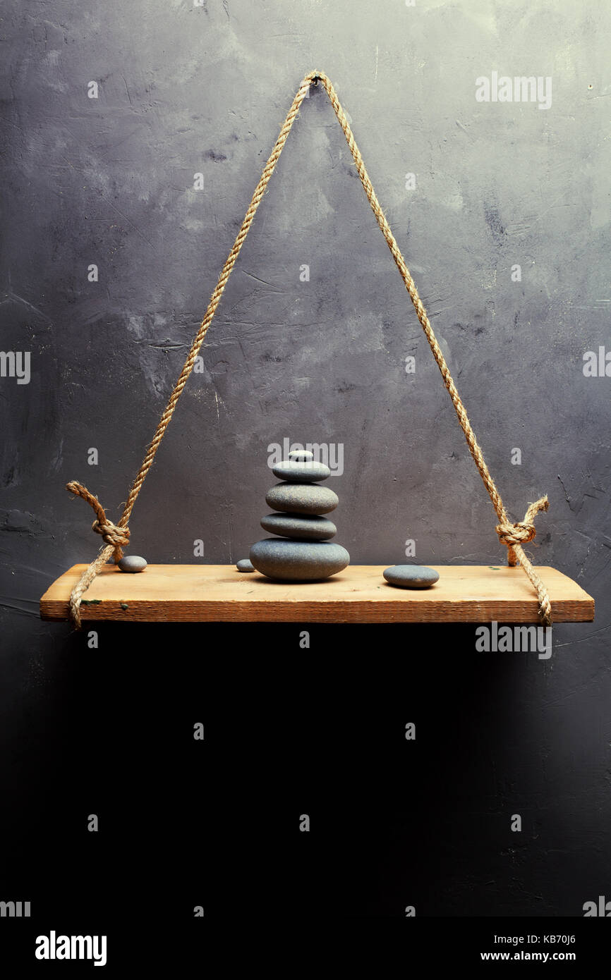 pyramid of pebbles on the old wood shelf hanging on rope on textured ...