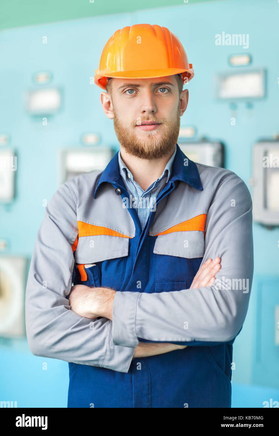 Portrait of young engineer at control room in factory. Crossed arms ...