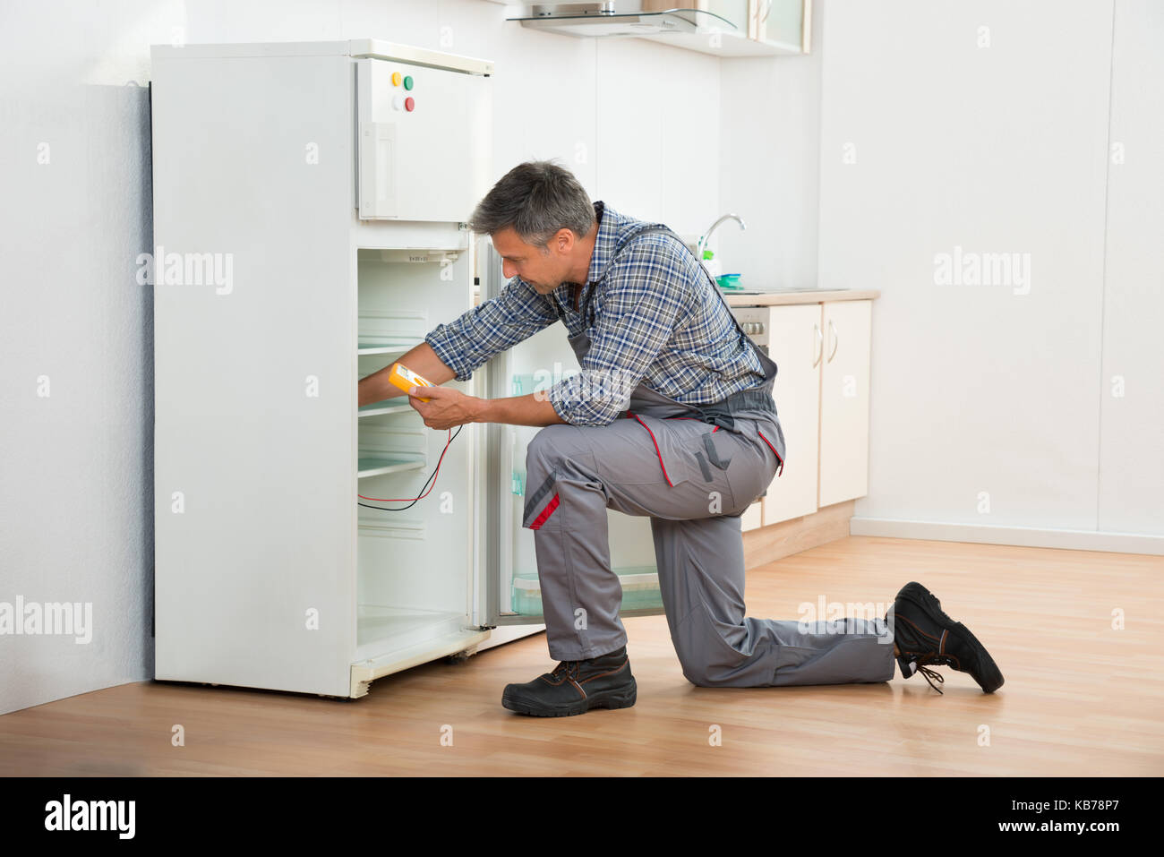 Mature male technician checking fridge with digital multimeter at home ...