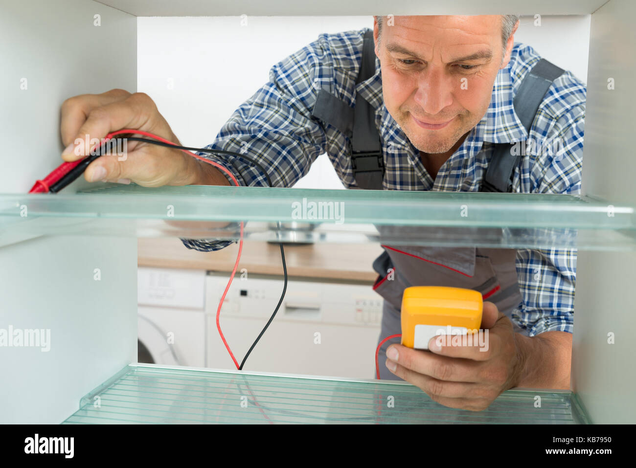 Male repairman checking fridge with digital multimeter at home Stock ...