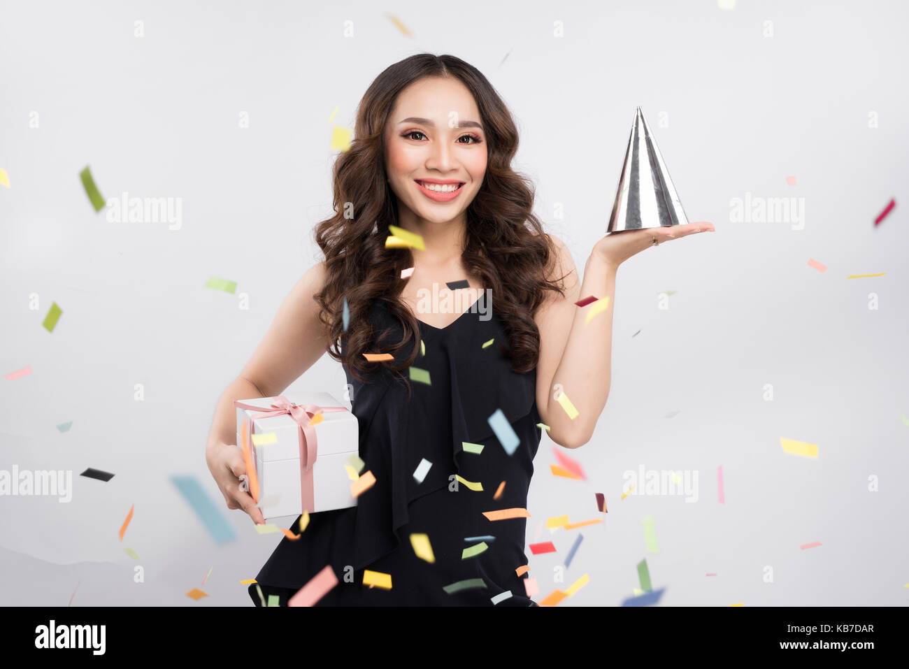 Happy asian woman celebrating holding gift box with confetti on white ...