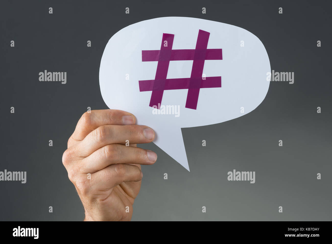 Closeup of hand showing hashtag on speech bubble against gray ...