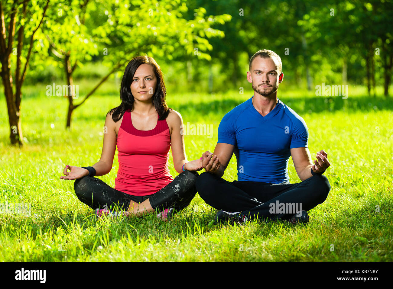 Young man and woman doing yoga in the sunny summer park Stock Photo - Alamy