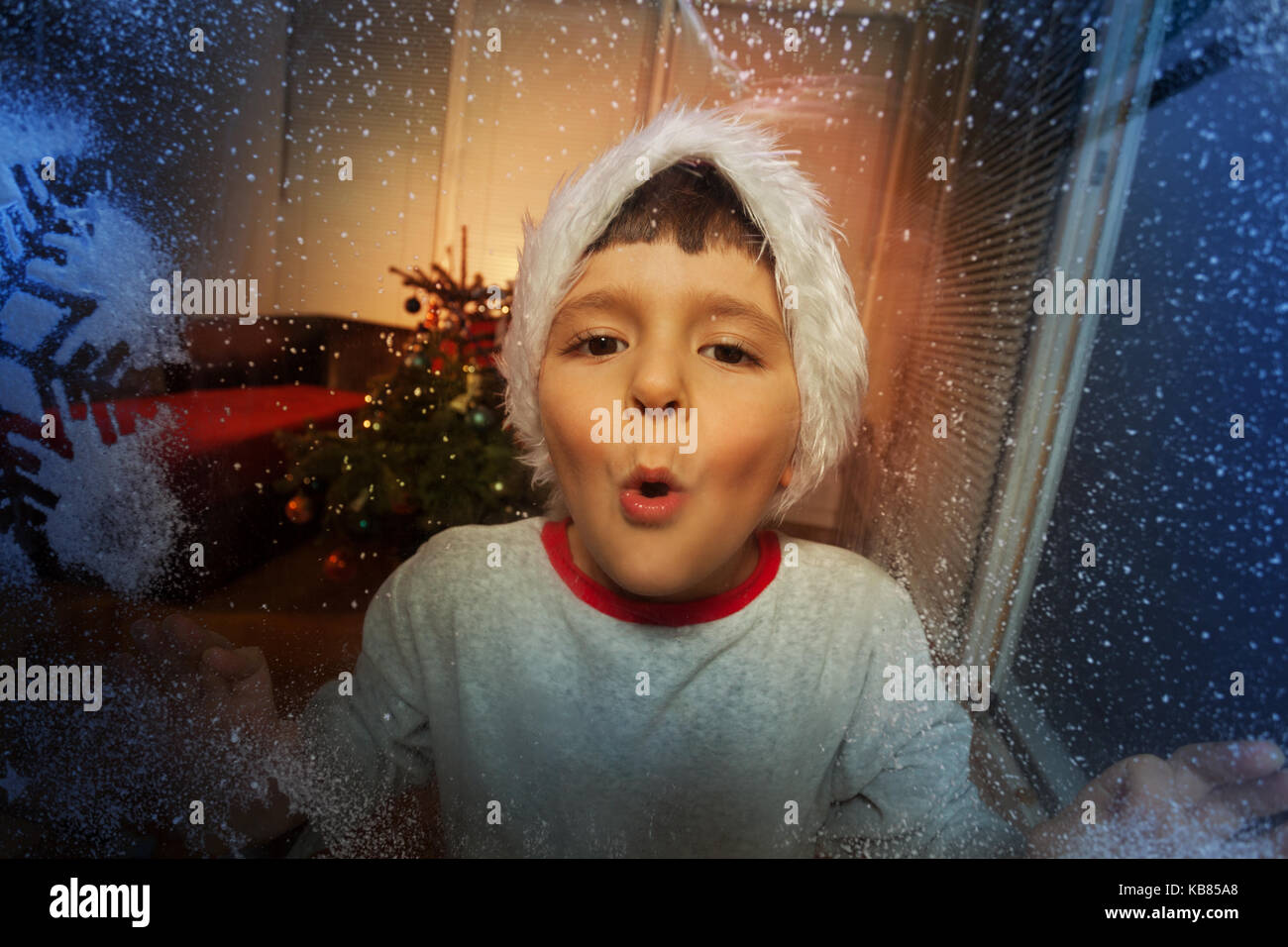 Little boy blowing on frosty window with snowflake Stock Photo - Alamy