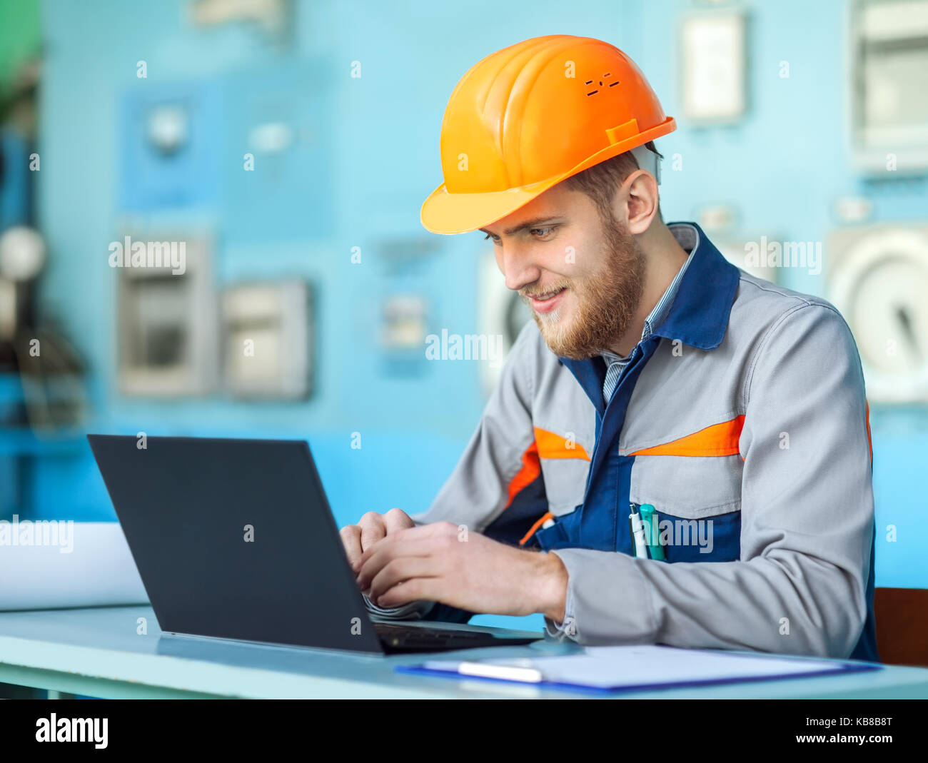 Portrait of young happy engineer working at laptop in control room ...
