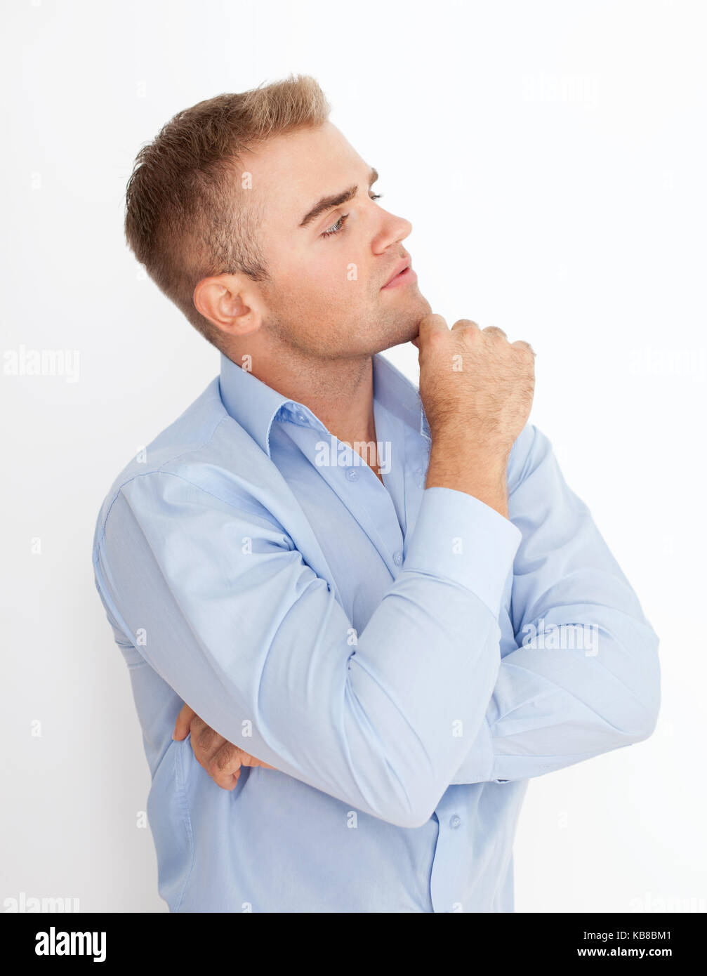 Portrait of young business man holding hand up to chin with arms folded ...