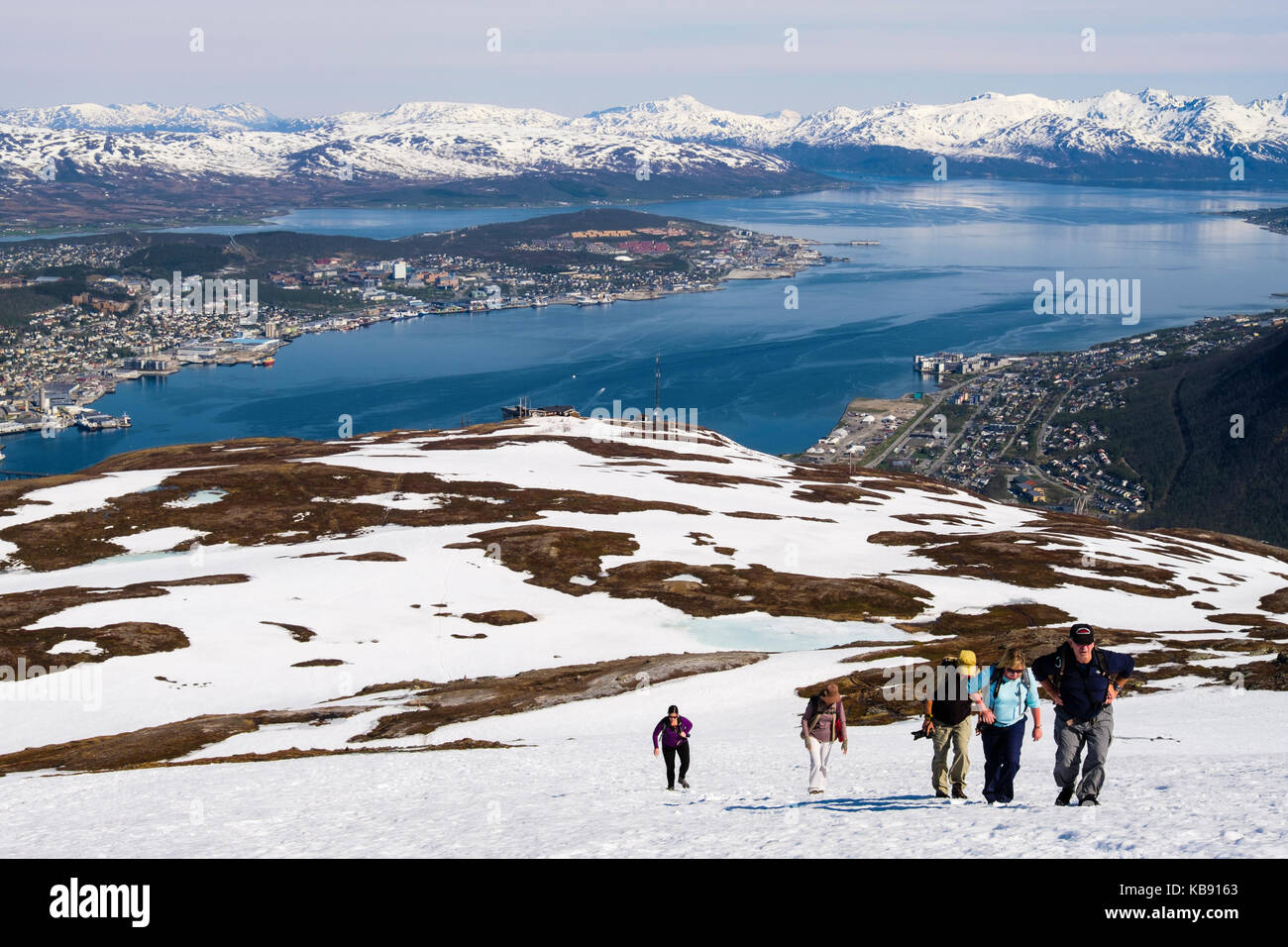 Hikers walking through snow on Mount Storsteinen with view to city on ...