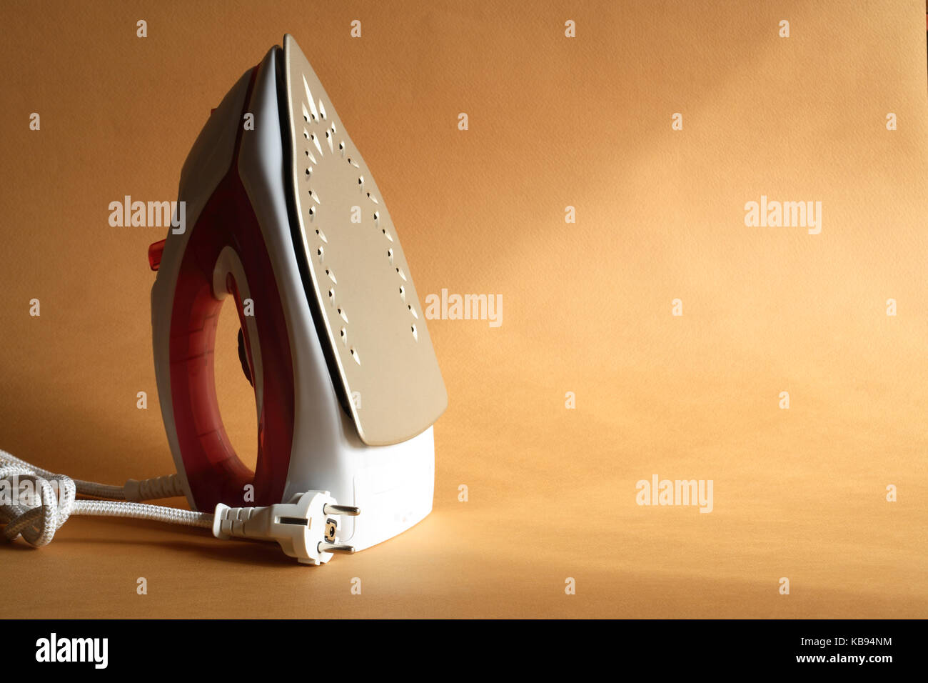 Modern electric iron standing on nice gold background with sun lighting ...