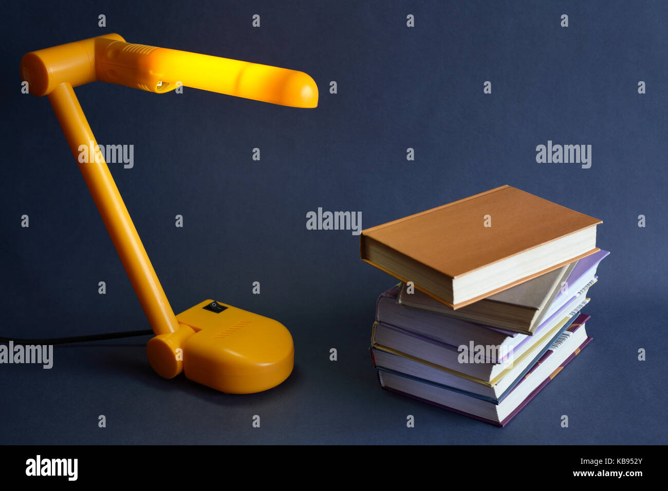 Stack of books near luminous modern desk lamp on dark background Stock ...