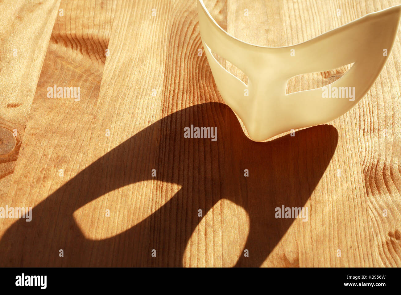 White plastic venetian mask lying on wooden surface with sunbeam and ...
