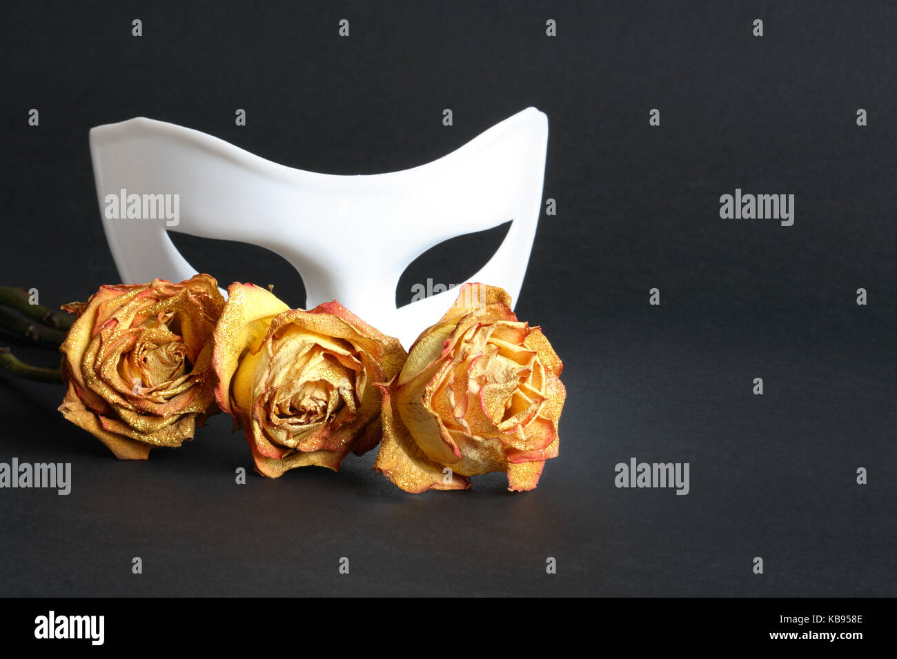 White venetian mask and dry yellow roses on black background Stock ...