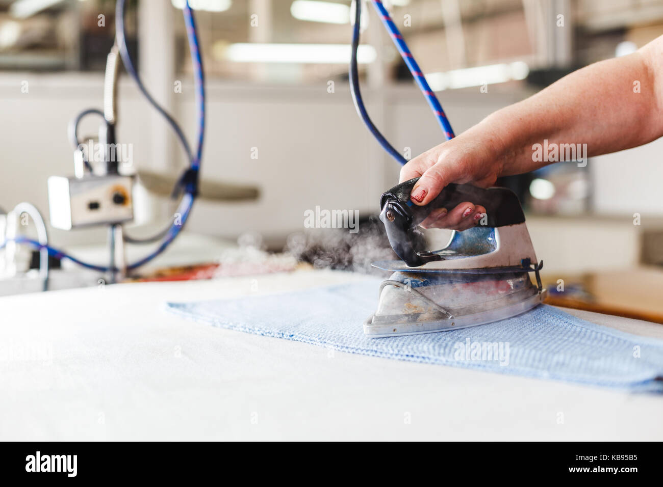 Close up of professional iron in a tailors factory. Woman hand ironing ...