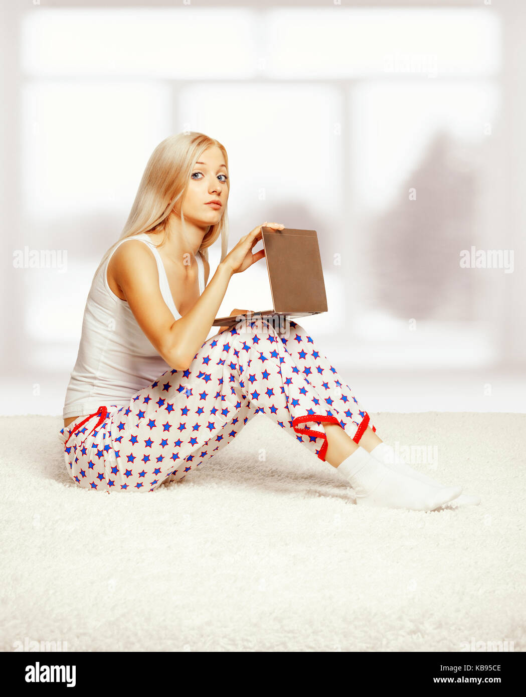 Young blonde woman in pyjamas on white whole-floor carpet browsing ...