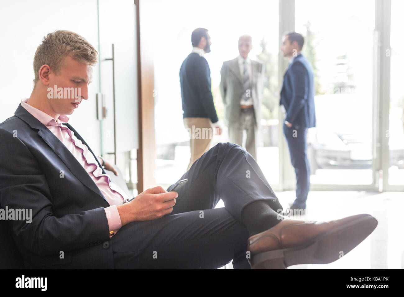 Businessman using smart phone while sitting in waiting room Stock Photo ...